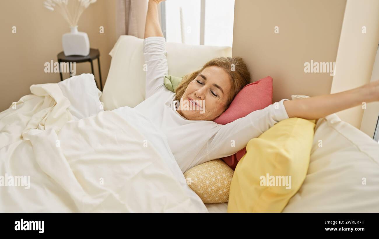 A serene adult woman stretching in bed with a peaceful expression in a ...