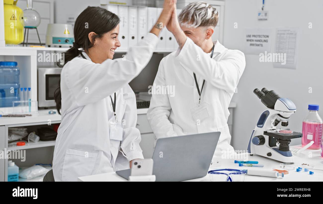 A man and woman, both scientists, joyfully high-five each other in a ...