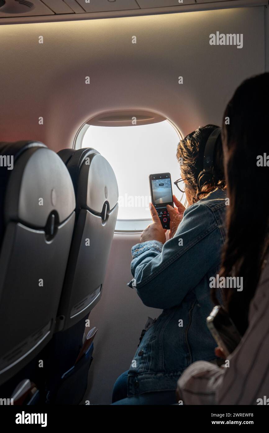 A vertical shot of a young woman taking a photo from an airplane window ...