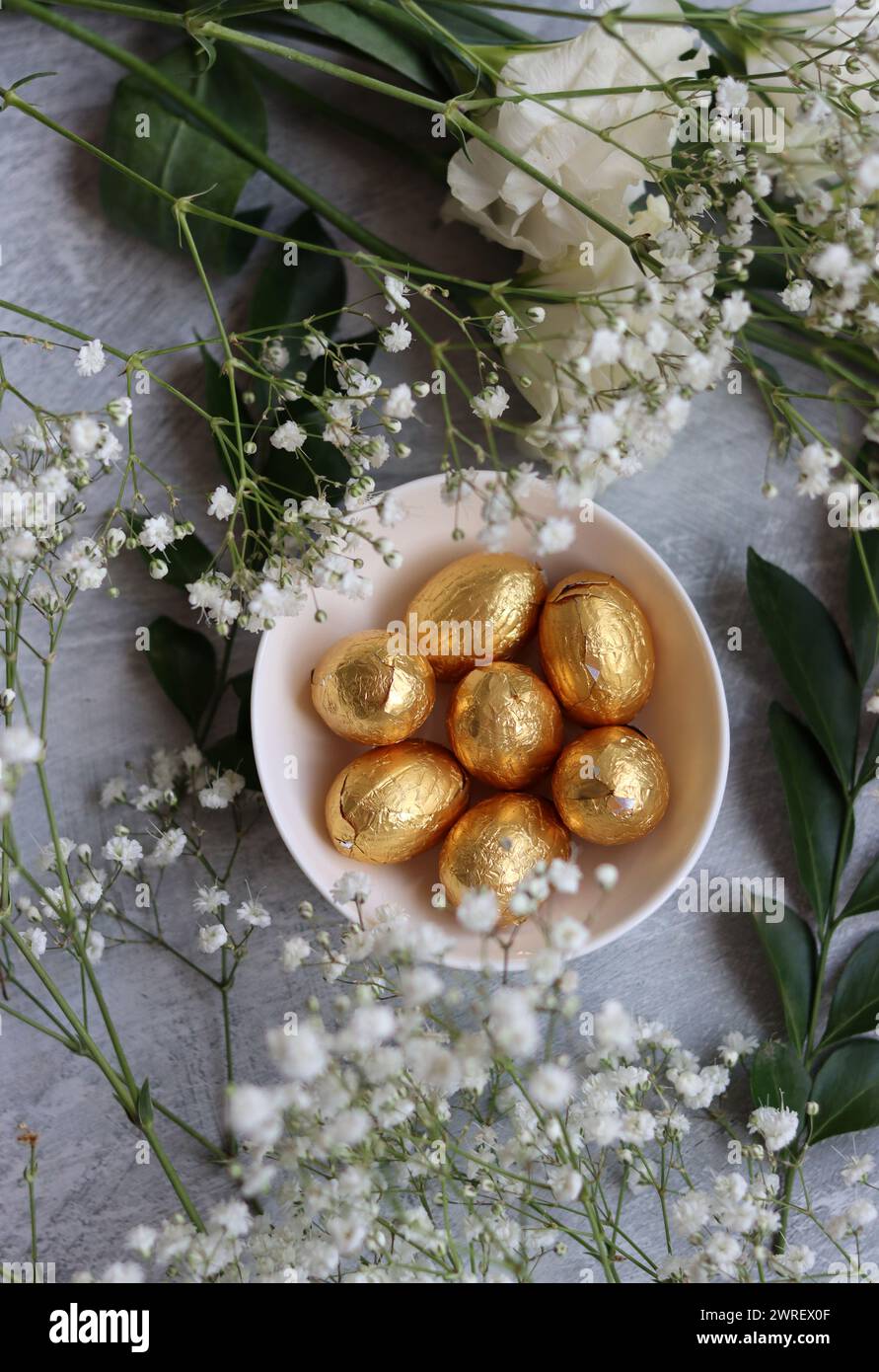 Chocolate Easter Egg Wrapped in Gold Foil. White spring flowers and ...