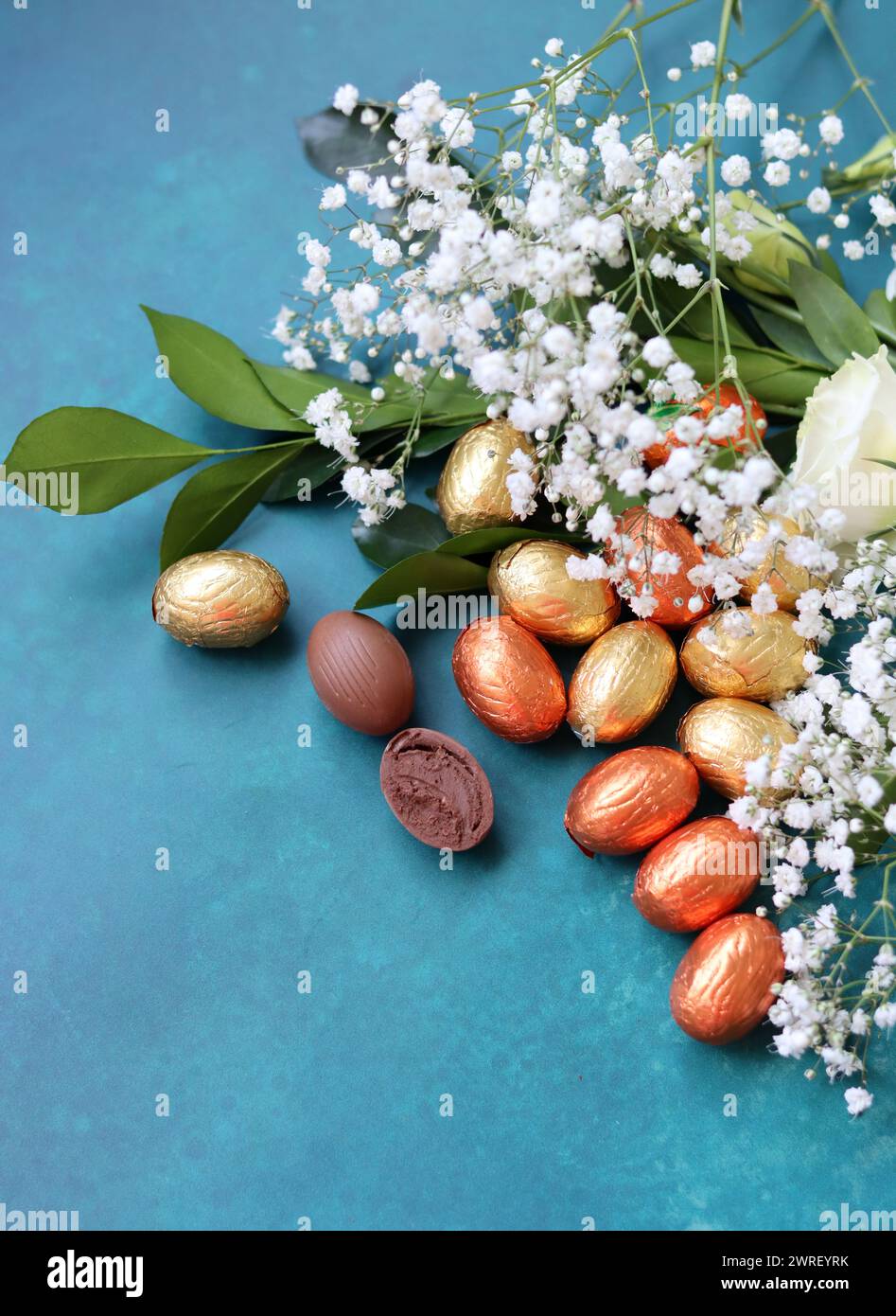 Chocolate Easter Egg Wrapped in Gold Foil. White spring flowers and ...