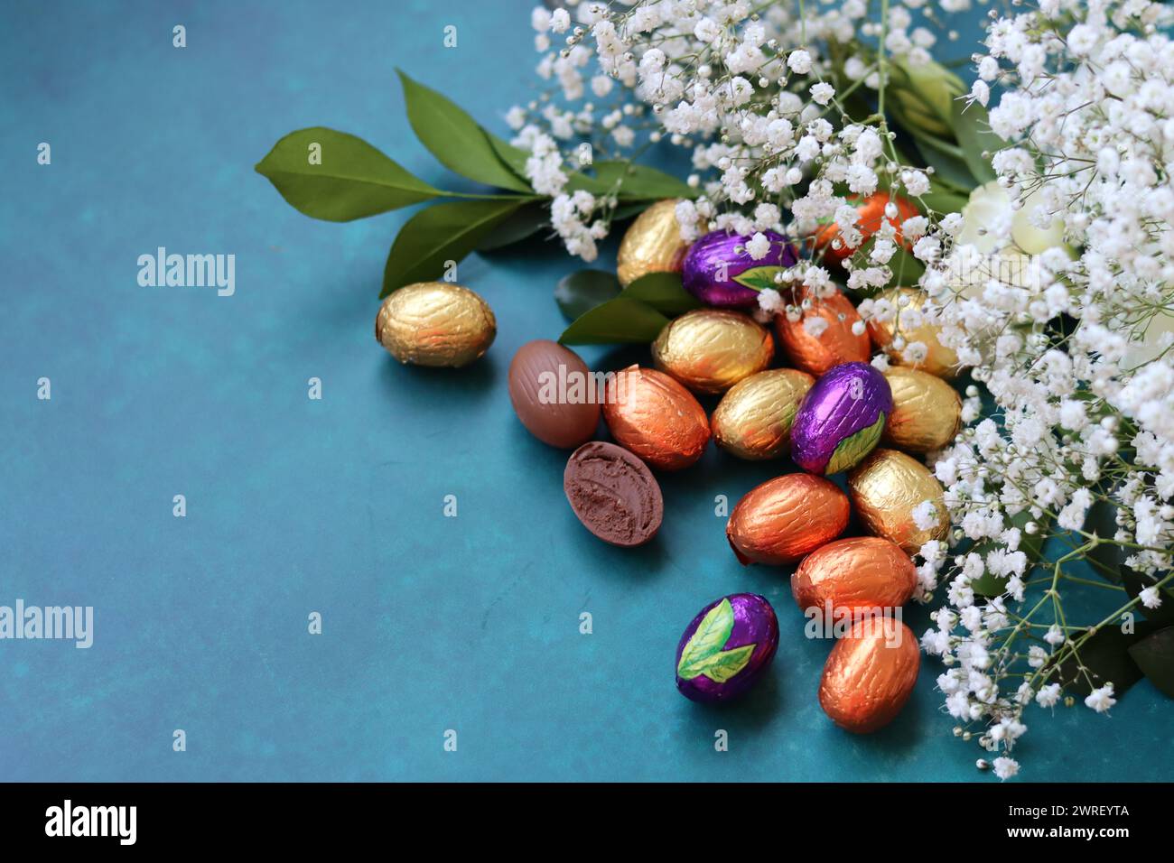 Chocolate Easter Egg Wrapped in Gold Foil. White spring flowers and ...