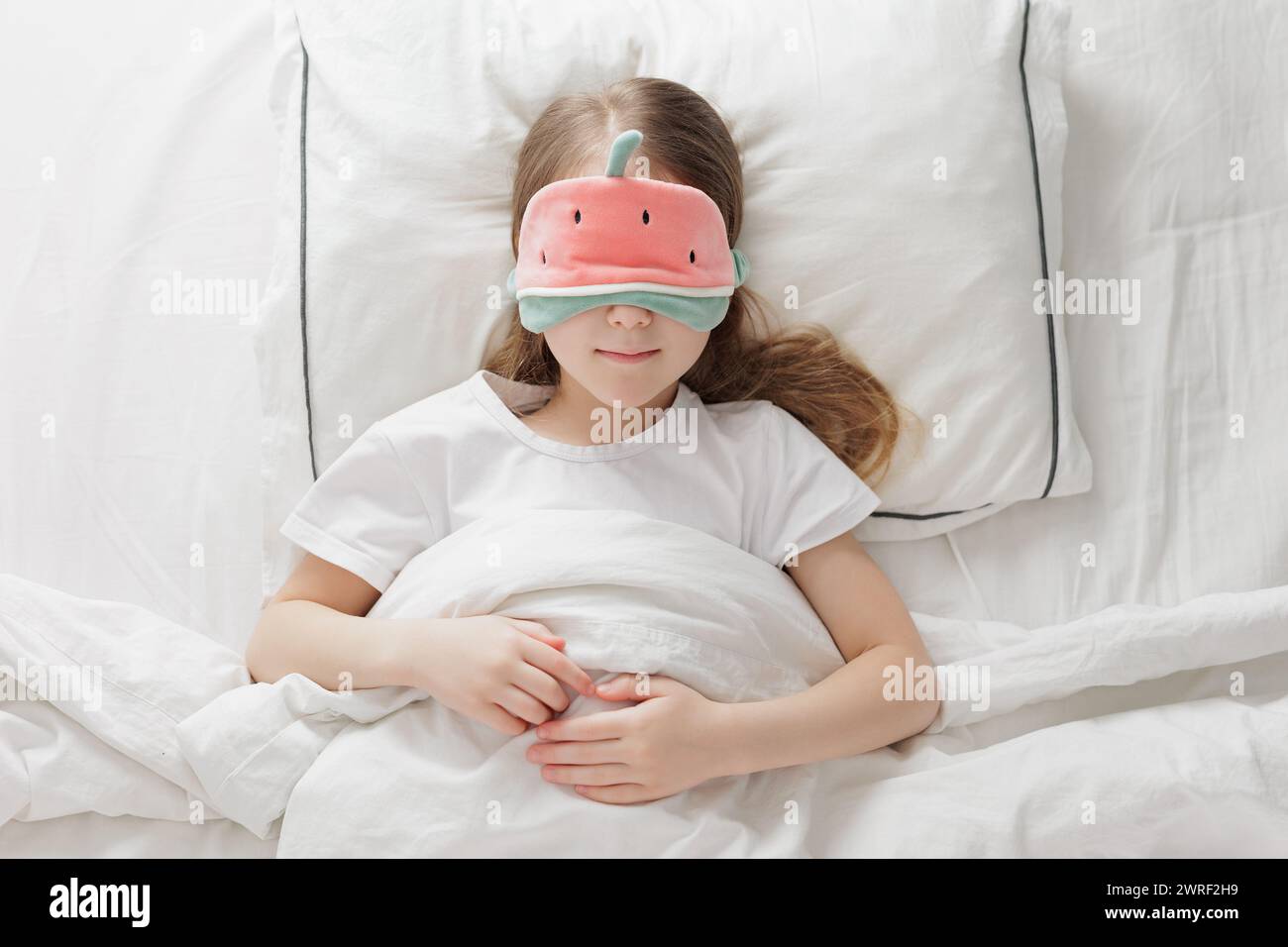 top view of cute little girl sleeping in watermelon mask in bed under ...