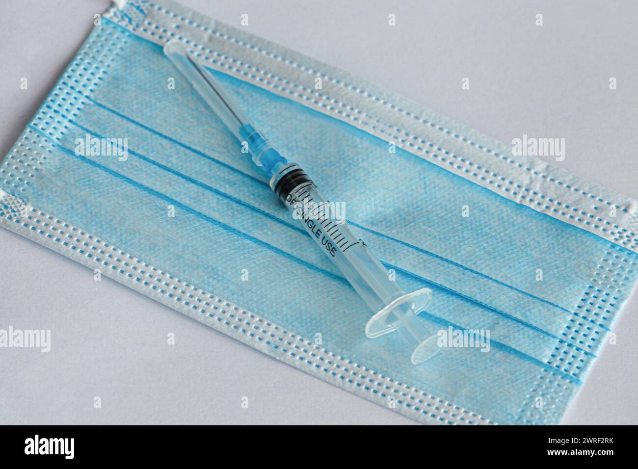 A syringe and face mask on white background - Top view. The syringe is ...