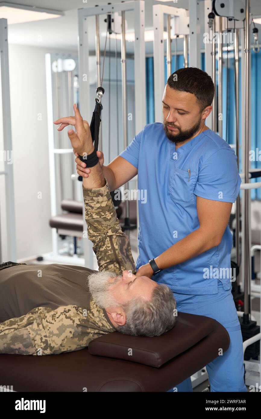 Physiotherapist helps military man perform exercises to stretch his arm ...