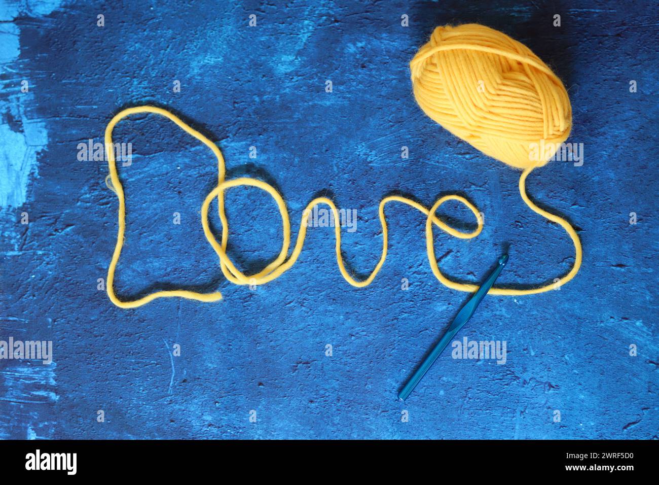 Word Love made of yellow wool tread on blue textured background with ...