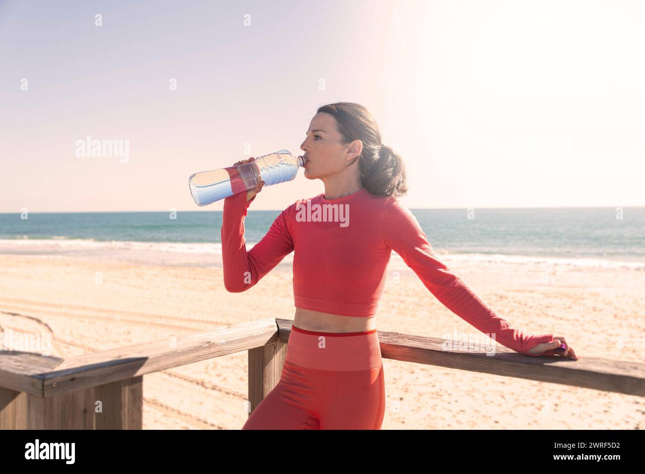 sporty woman taking a break to hydrate during exercise on the beach ...