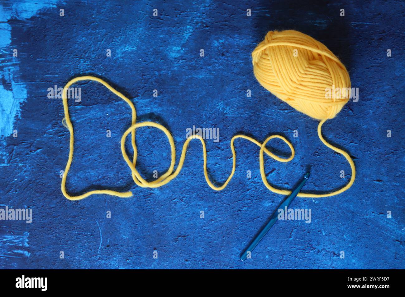 Word Love made of yellow wool tread on blue textured background with ...