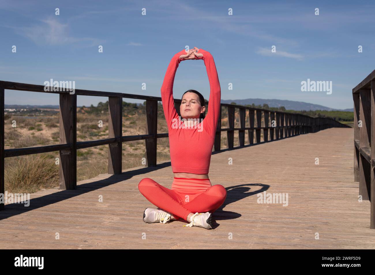 Sporty woman sitting cross legged doing an arm stretch warm up exercise ...