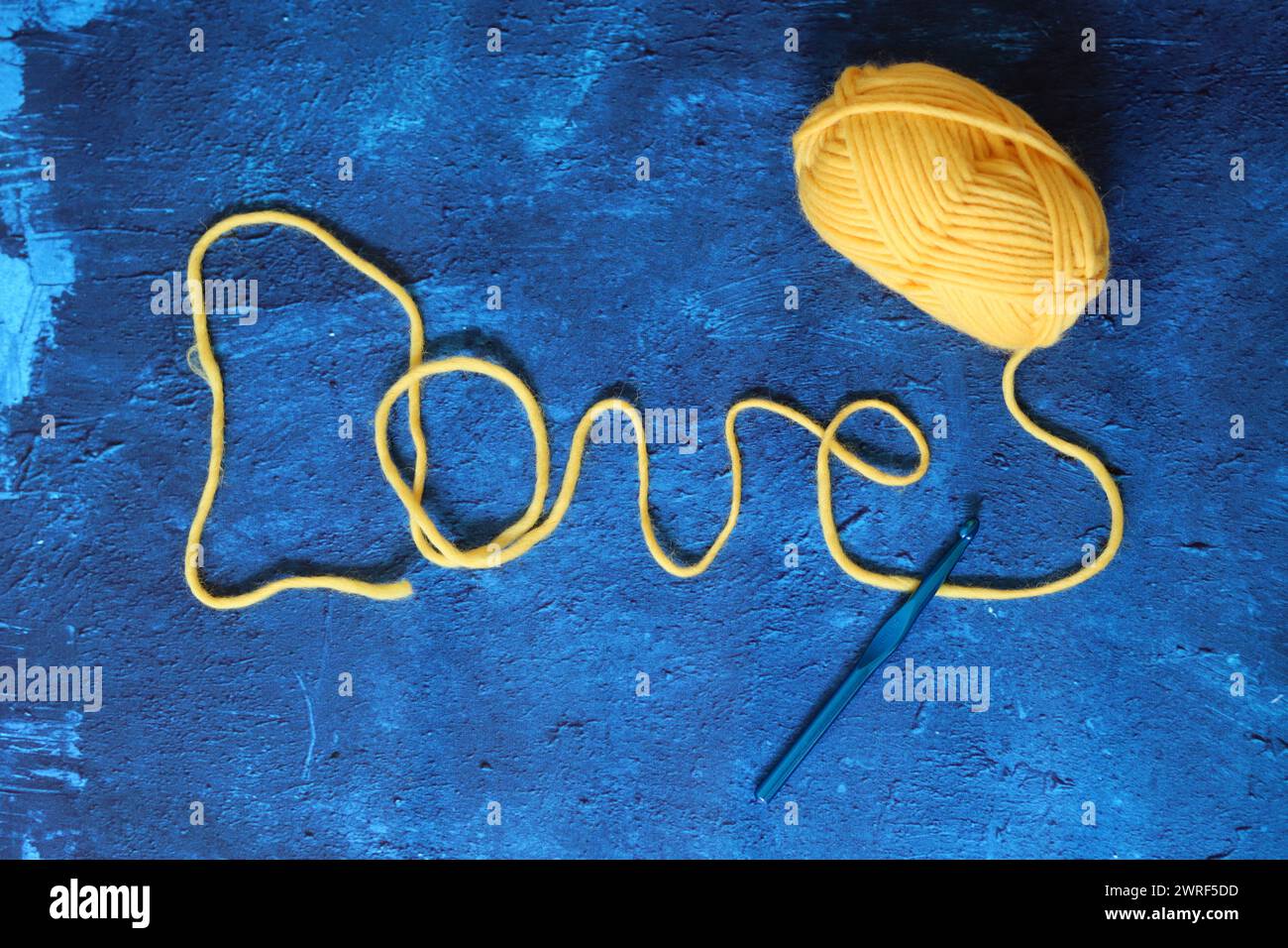 Word Love made of yellow wool tread on blue textured background with ...