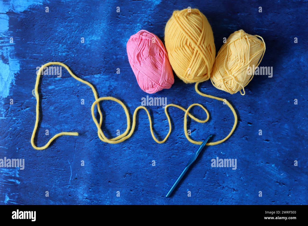 Word Love made of yellow wool tread on blue textured background with ...