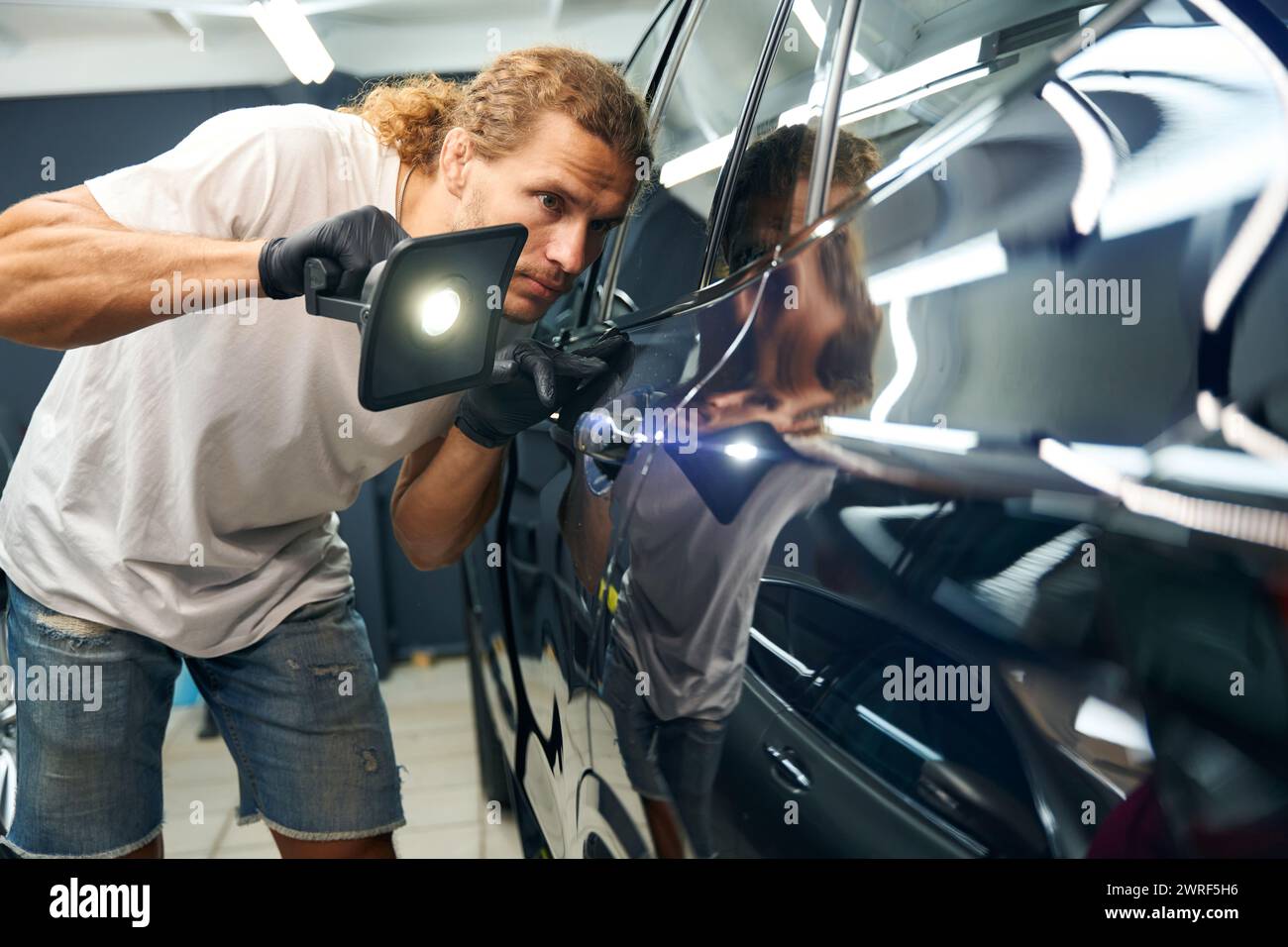Master in a car repair shop conducts control inspection of car body ...