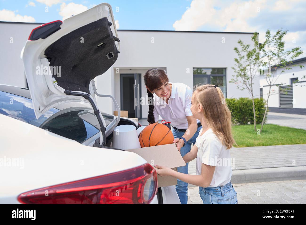 Mother and daughter taking box from car trunk during moving to ...