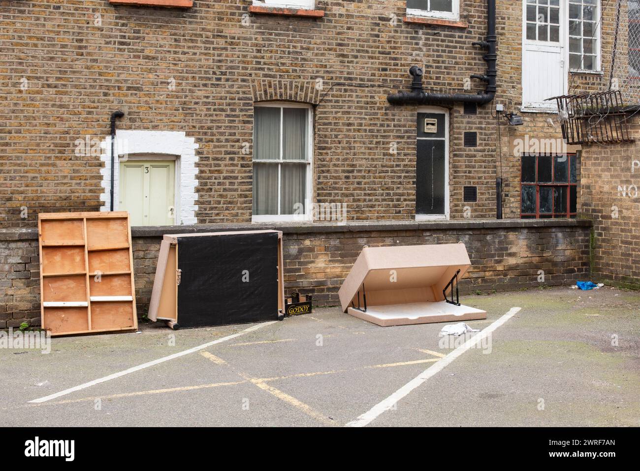 A carpark with broken bits of a dismantled bed with lift-up and drawer ...