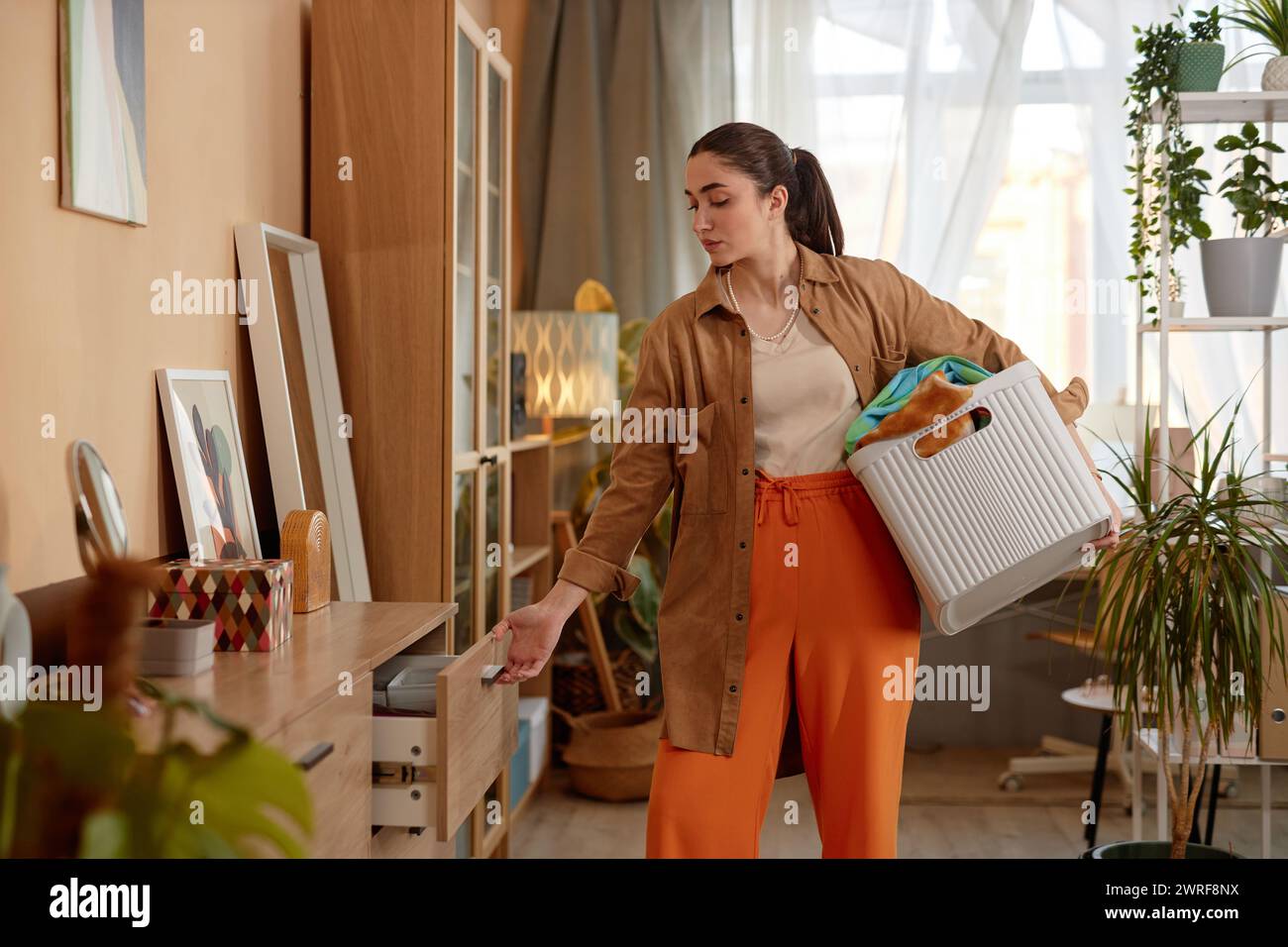 Side view portrait of young woman putting away clean clothes on laundry ...