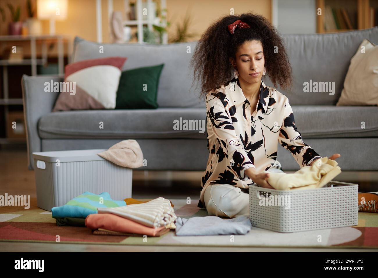 Portrait of young African American woman folding and putting away clean ...