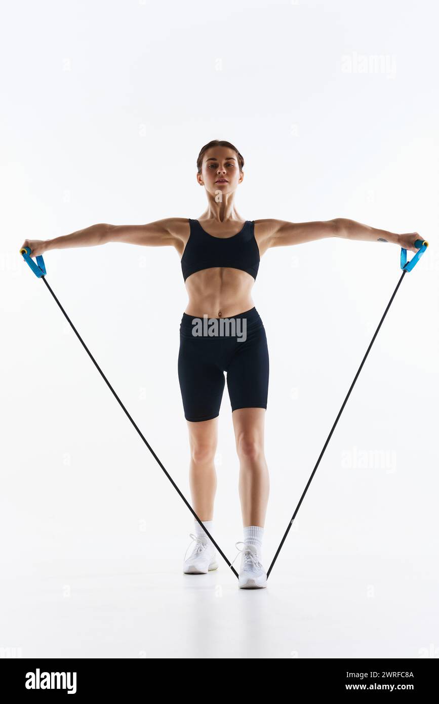 Fit young woman in black sportswear training, using resistance bands ...
