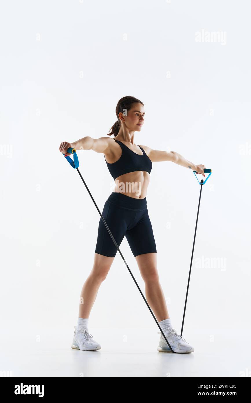 Fit young woman in black sportswear training, using resistance bands ...
