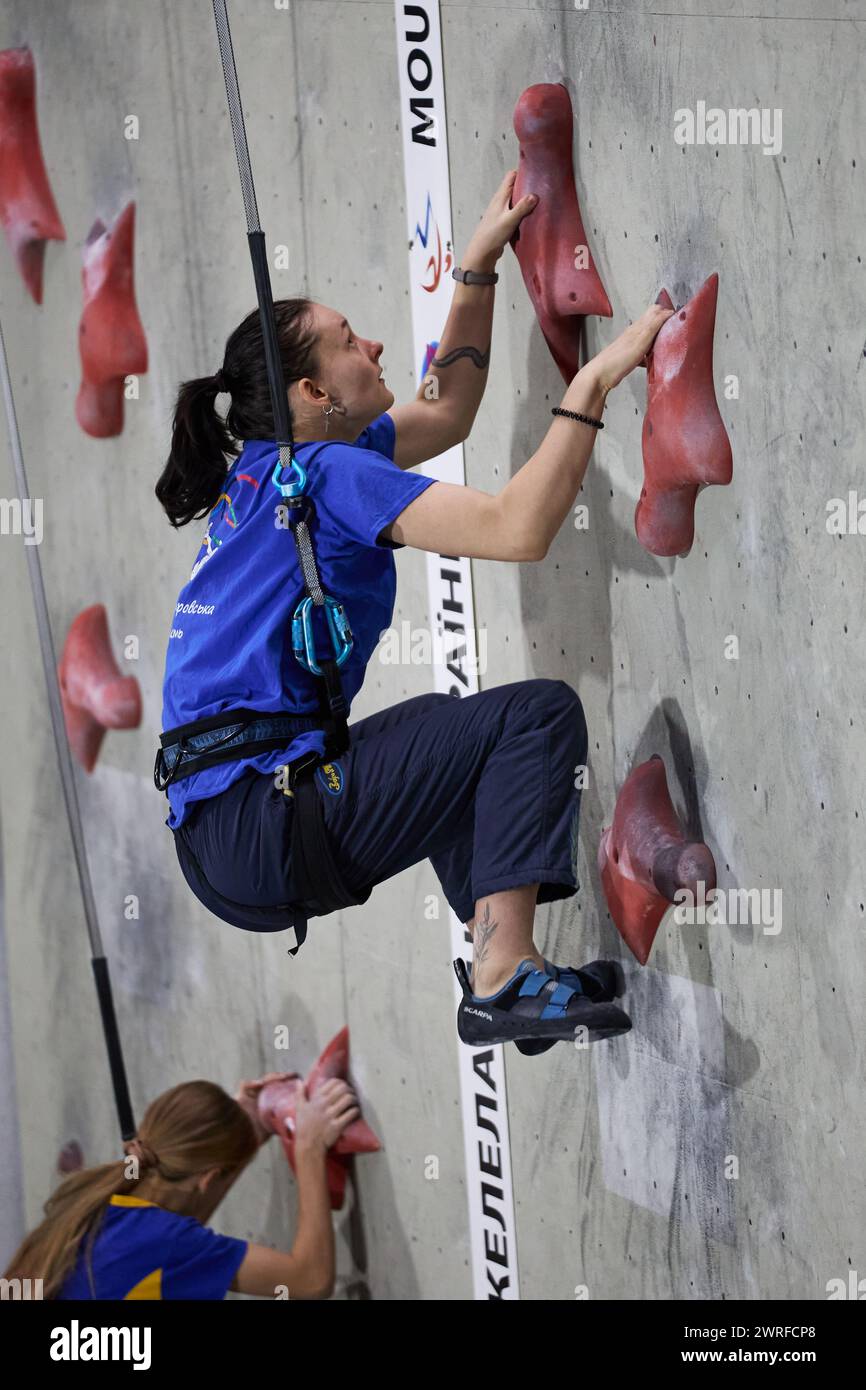 Female climber hangs on a vertical wall at a speed climbing competition ...