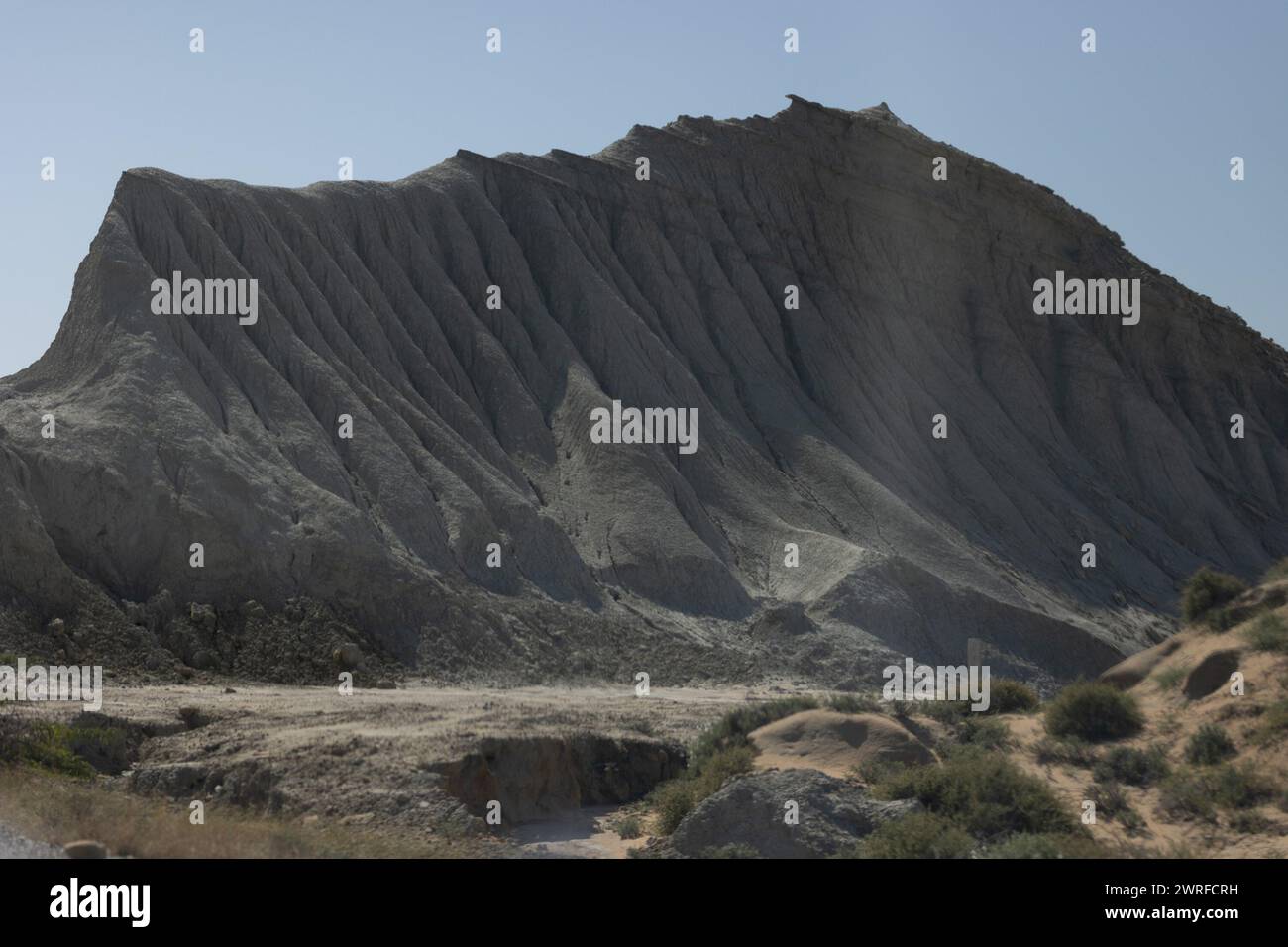 A barren mountain ridge with deeply eroded slopes stands under a clear ...