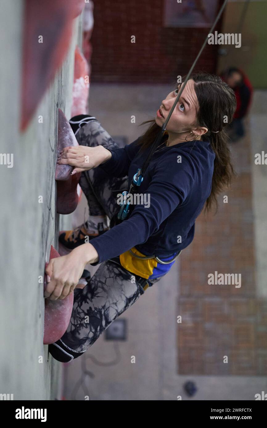 Strong young female athlete climbs the vertical wall at a professional ...