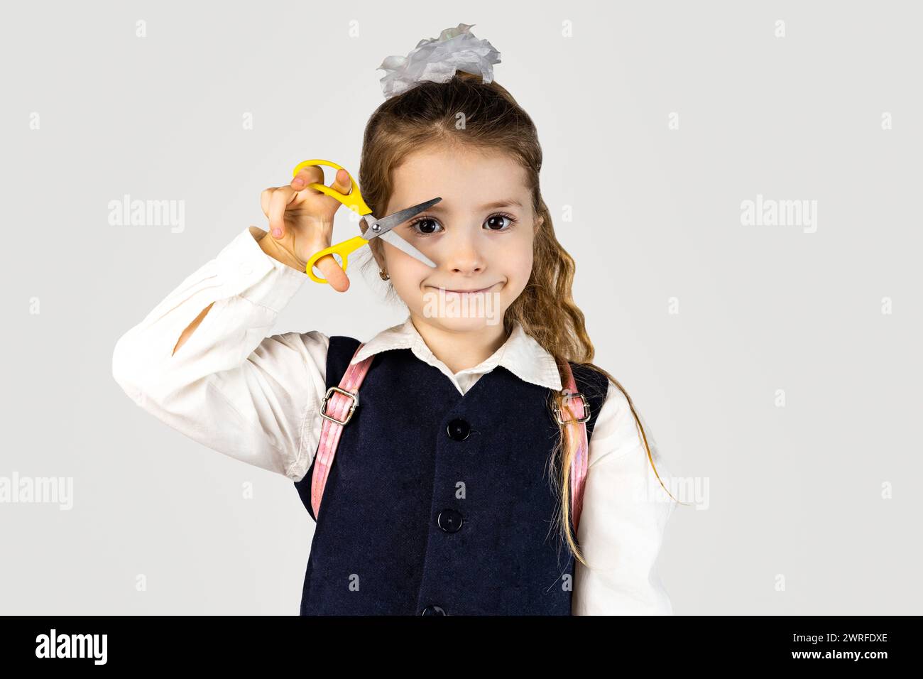 A little girl in a school uniform smiles happily, holding a pair of ...