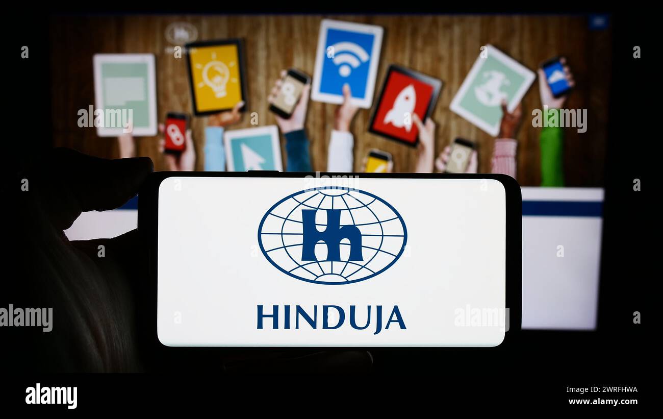 Person holding cellphone with logo of Indian conglomerate Hinduja Group Ltd. in front of ...