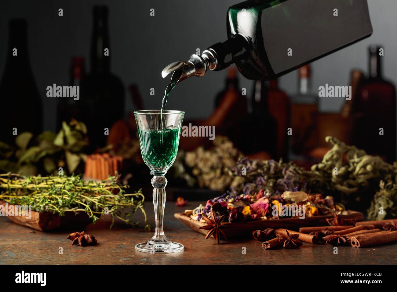 Green herbal liquor is poured from a vintage bottle into a glass. On a ...