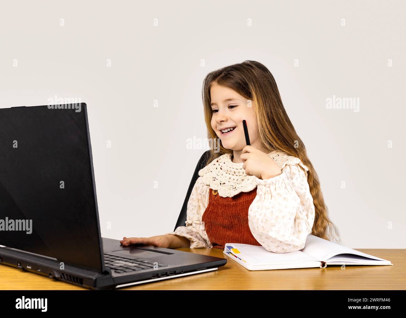 The young girl is seated at a desk, happily using a laptop computer ...