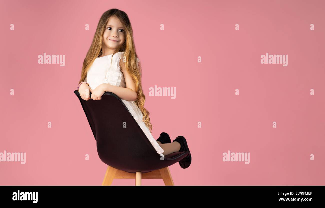 The happy little girl who is sitting on a black chair on a pink ...