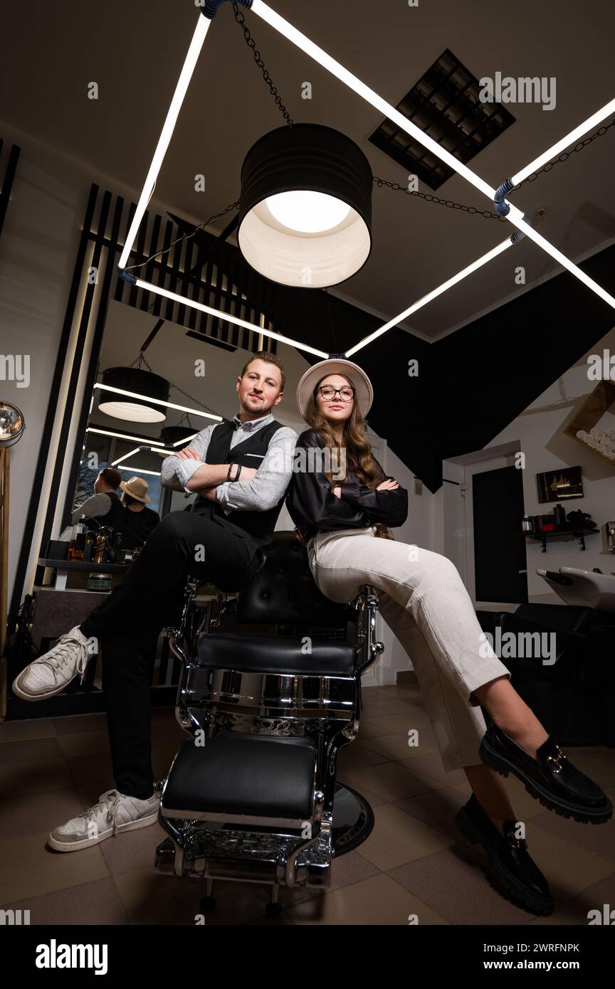 A couple of barbers sit side by side on a chair in a modern interior of ...