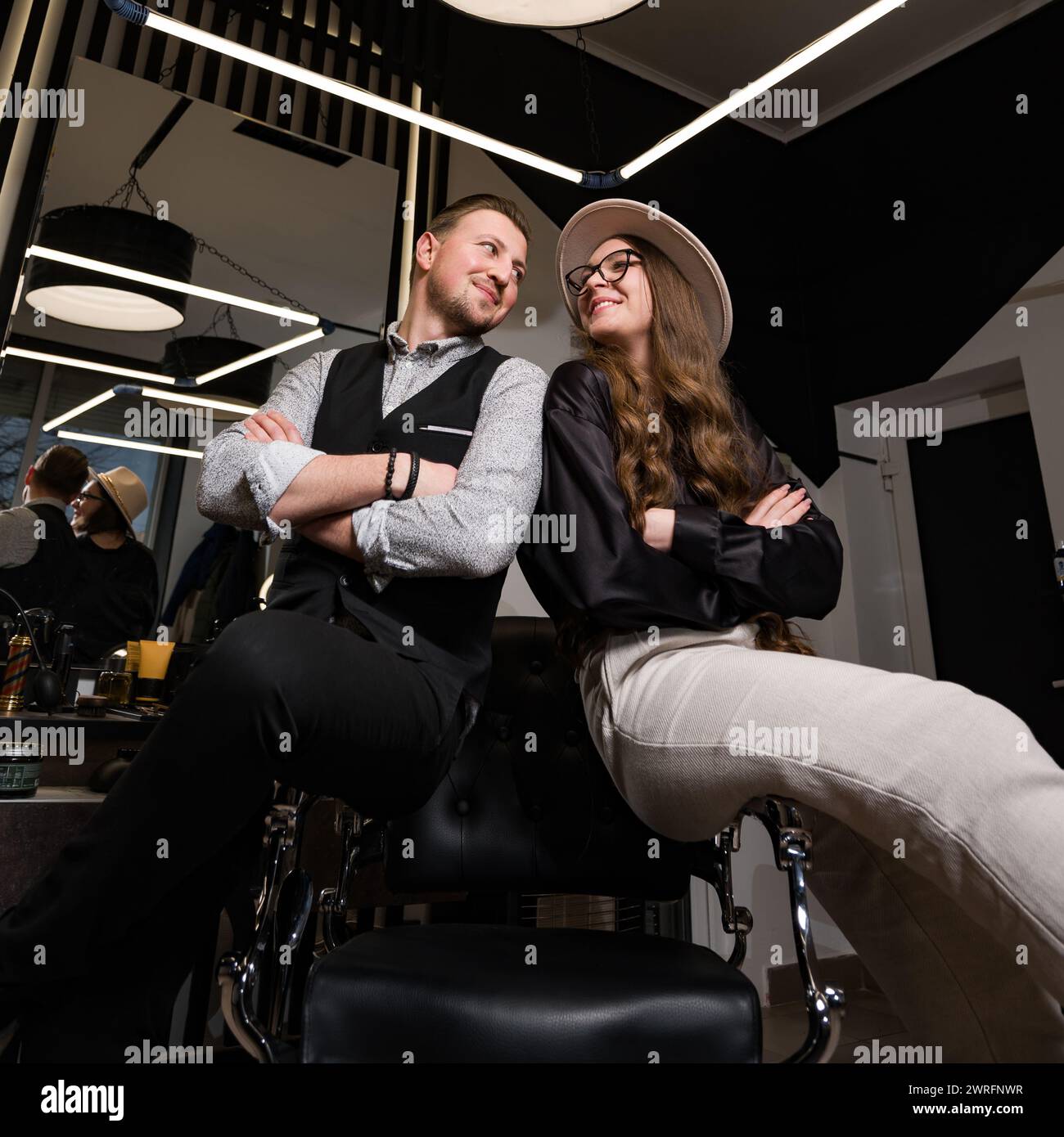 A couple of barbers look at each other sit side by side on a chair in a ...