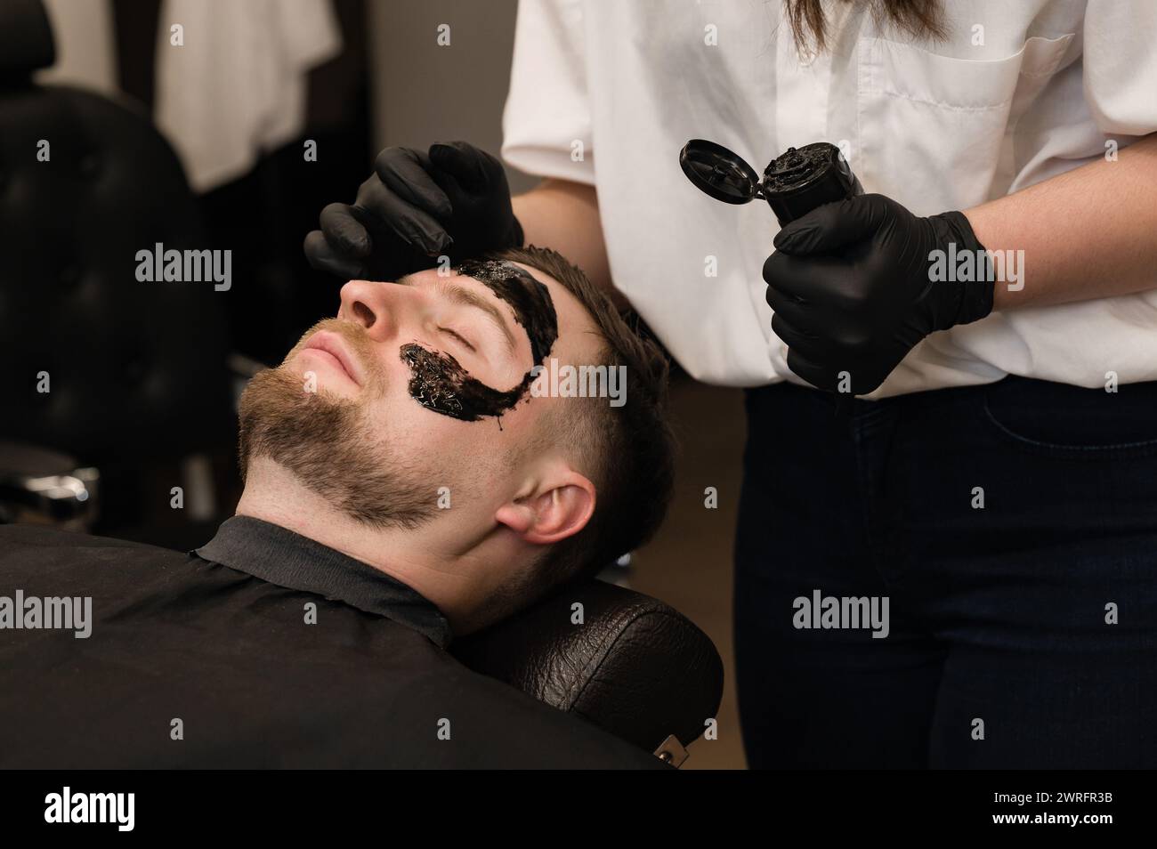 Barber applies a black moisturizing mask to a mans face while shaving ...