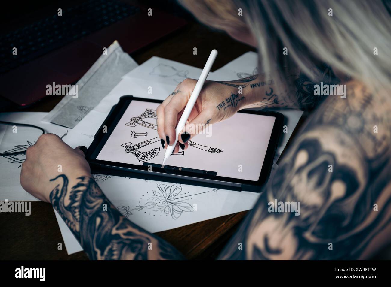 Horizontal photo a tattooed artist draws intricate designs on a tablet ...