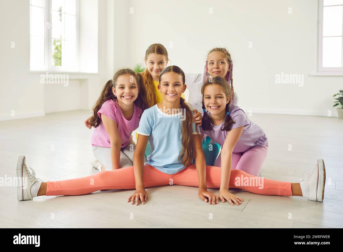 Group of happy flexible girls sitting on floor at sports school or ...
