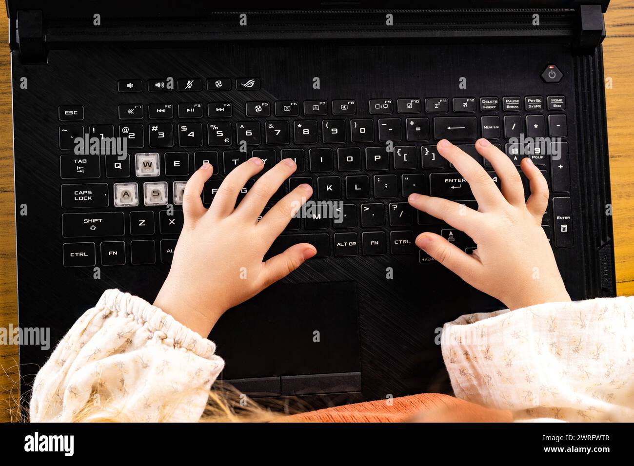 A young girl is using her fingernails to type on the keyboard of a laptop computer, utilizing ...