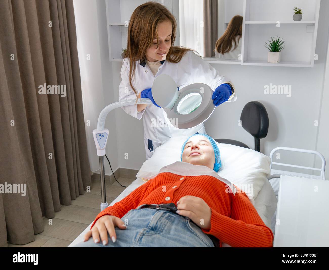 The dermatologist looks at the skin of the patient's face under the lamp. Cosmetologist or ...