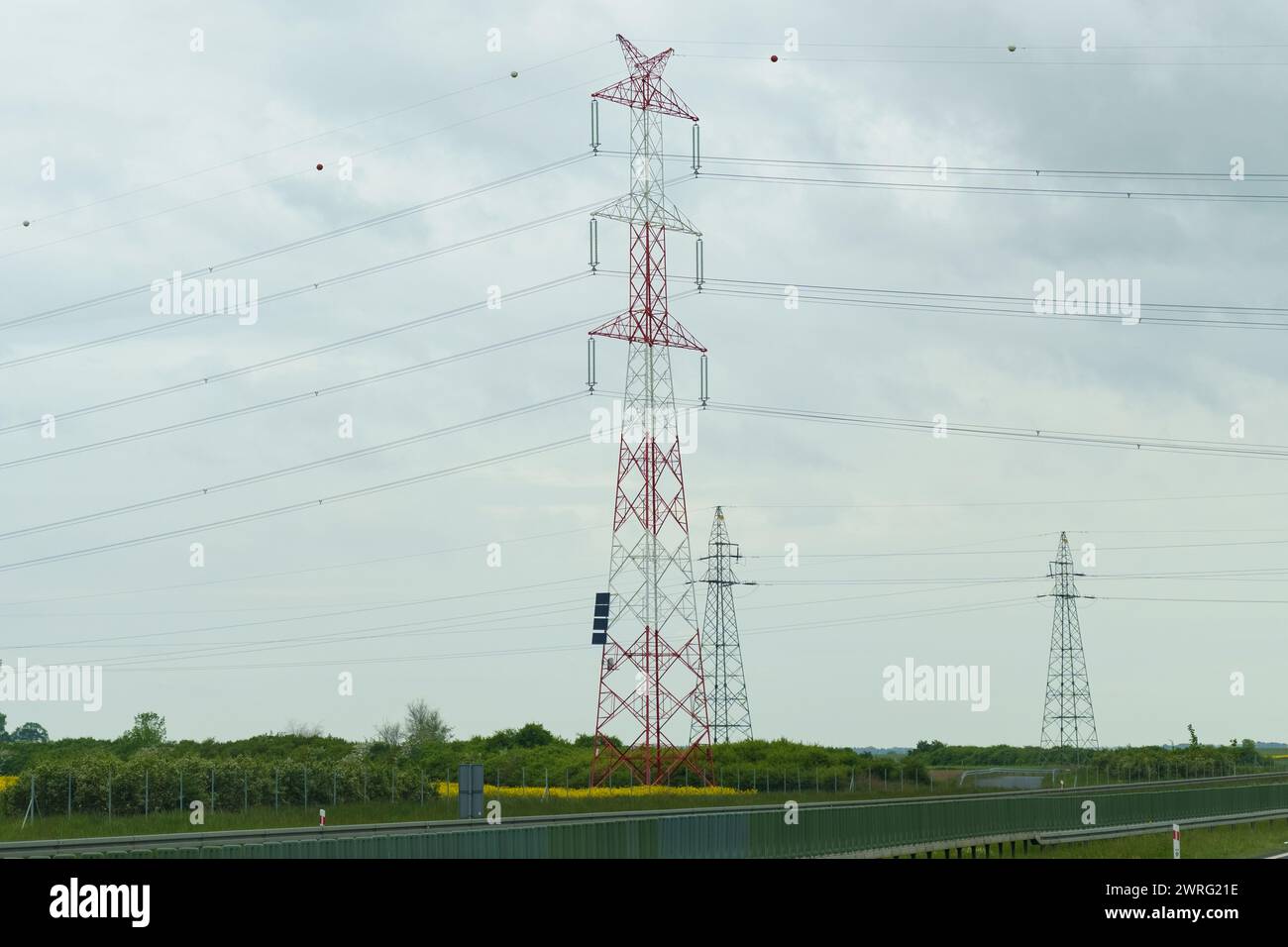 A high voltage power line towers against a clear blue sky, carrying ...