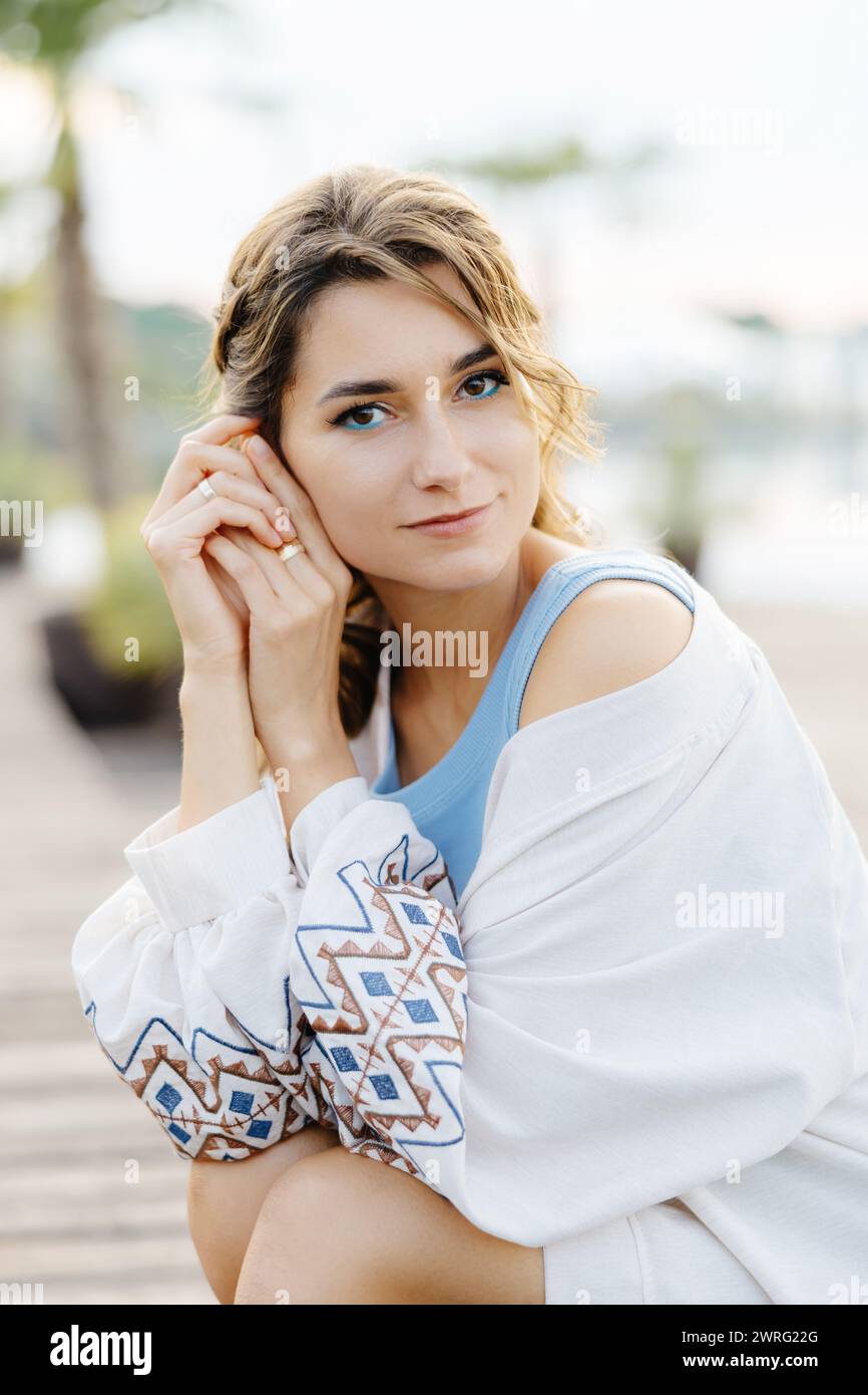 A woman is sitting on the ground outdoors, striking a pose for a photo ...