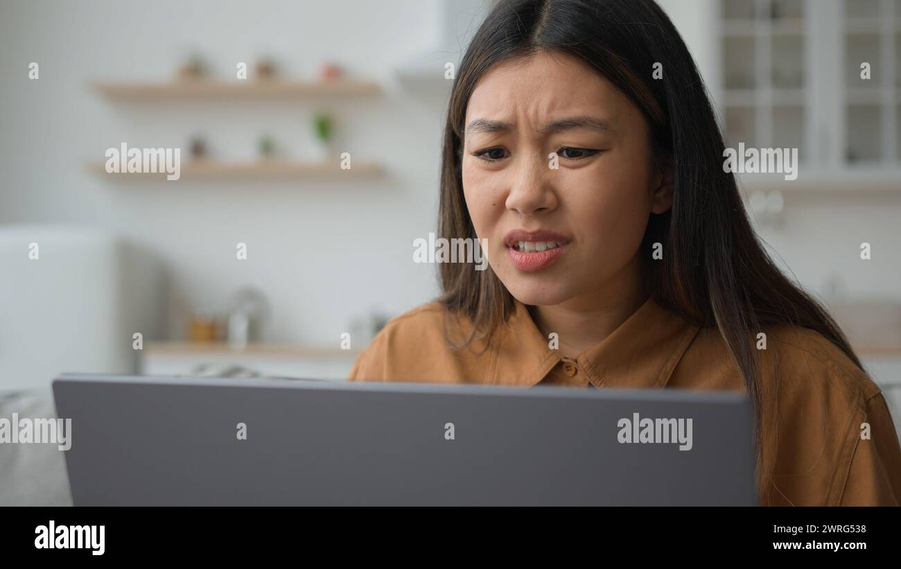 Angry upset Asian japanese woman girl homeowner using laptop in kitchen ...