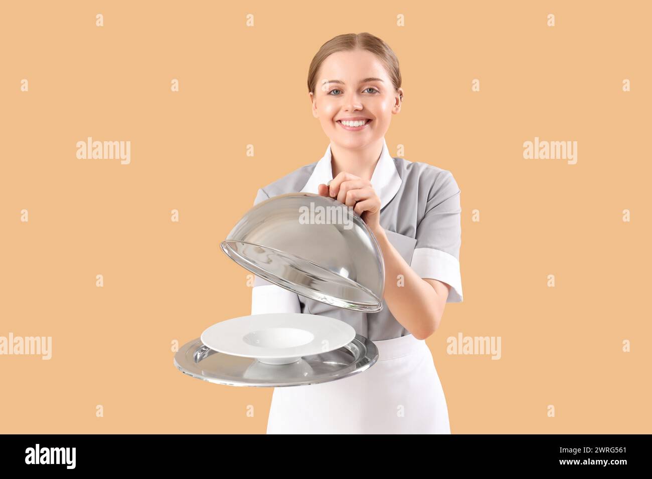 Young waitress with empty plate, tray and cloche on beige background ...