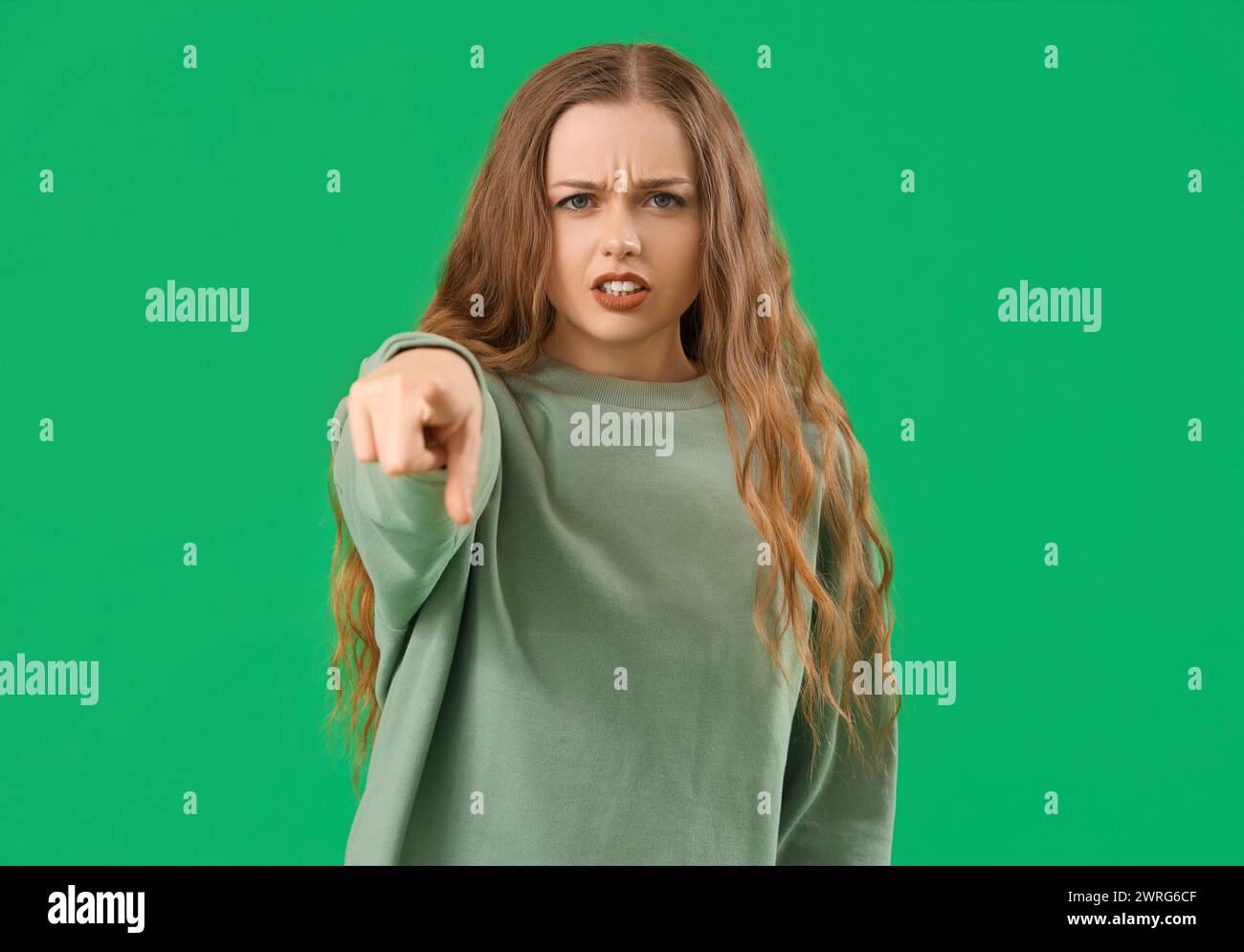 Young woman pointing at viewer on green background. Accusation concept ...