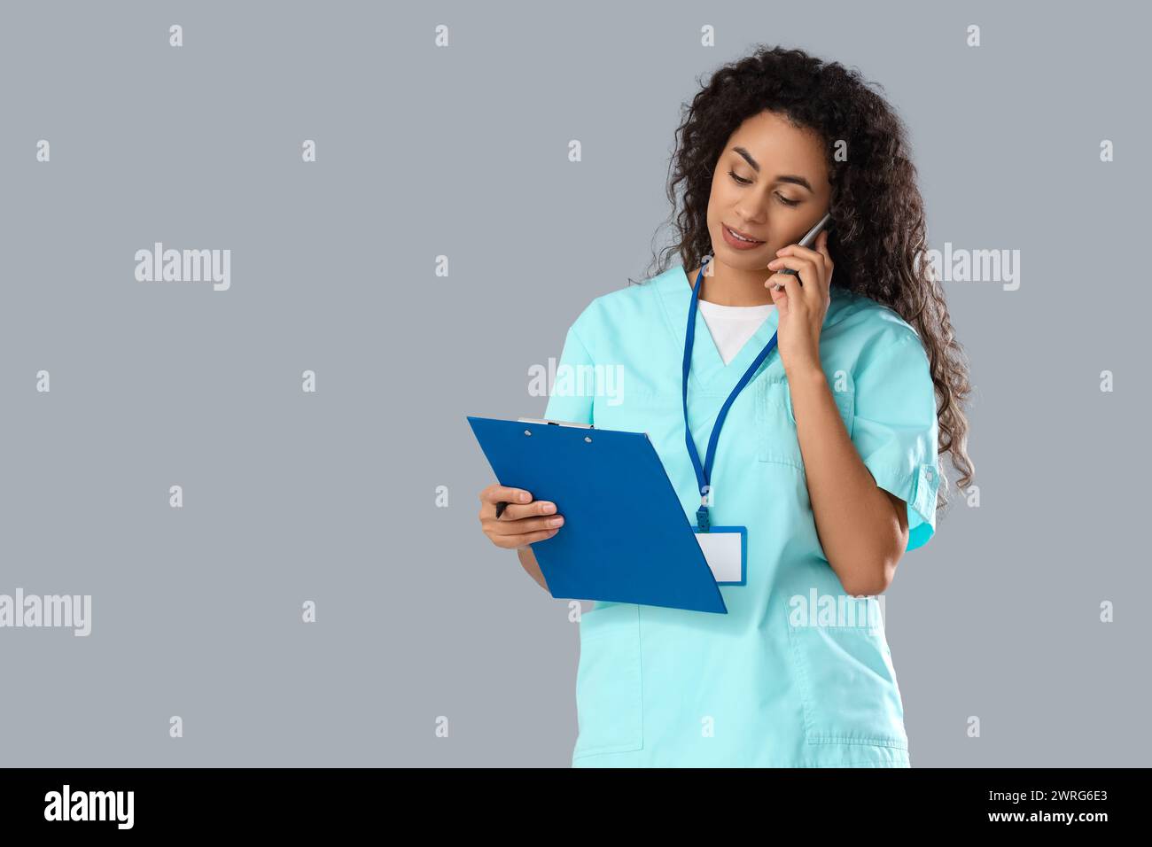 Female African-American medical intern with clipboard talking by mobile ...