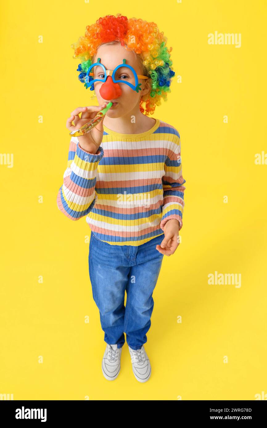Funny little girl in disguise with party blower on yellow background ...