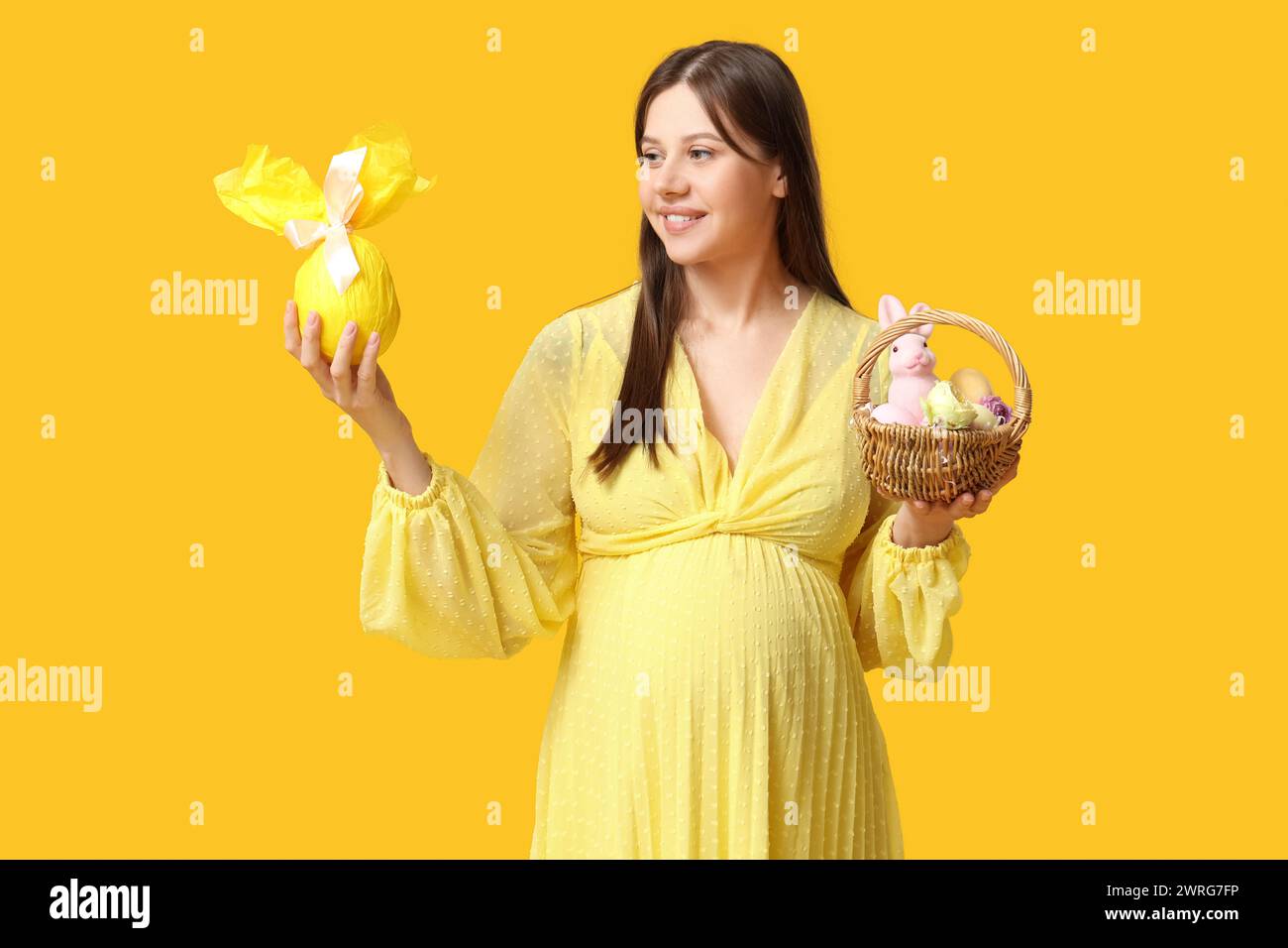 Beautiful young pregnant woman holding wicker basket with toy rabbit ...