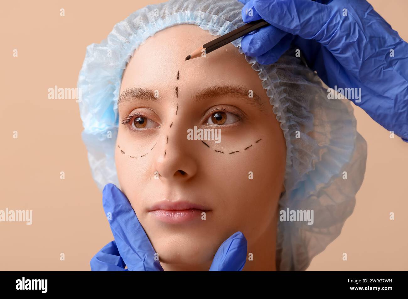 Plastic surgeon applying marks on female face against brown background ...