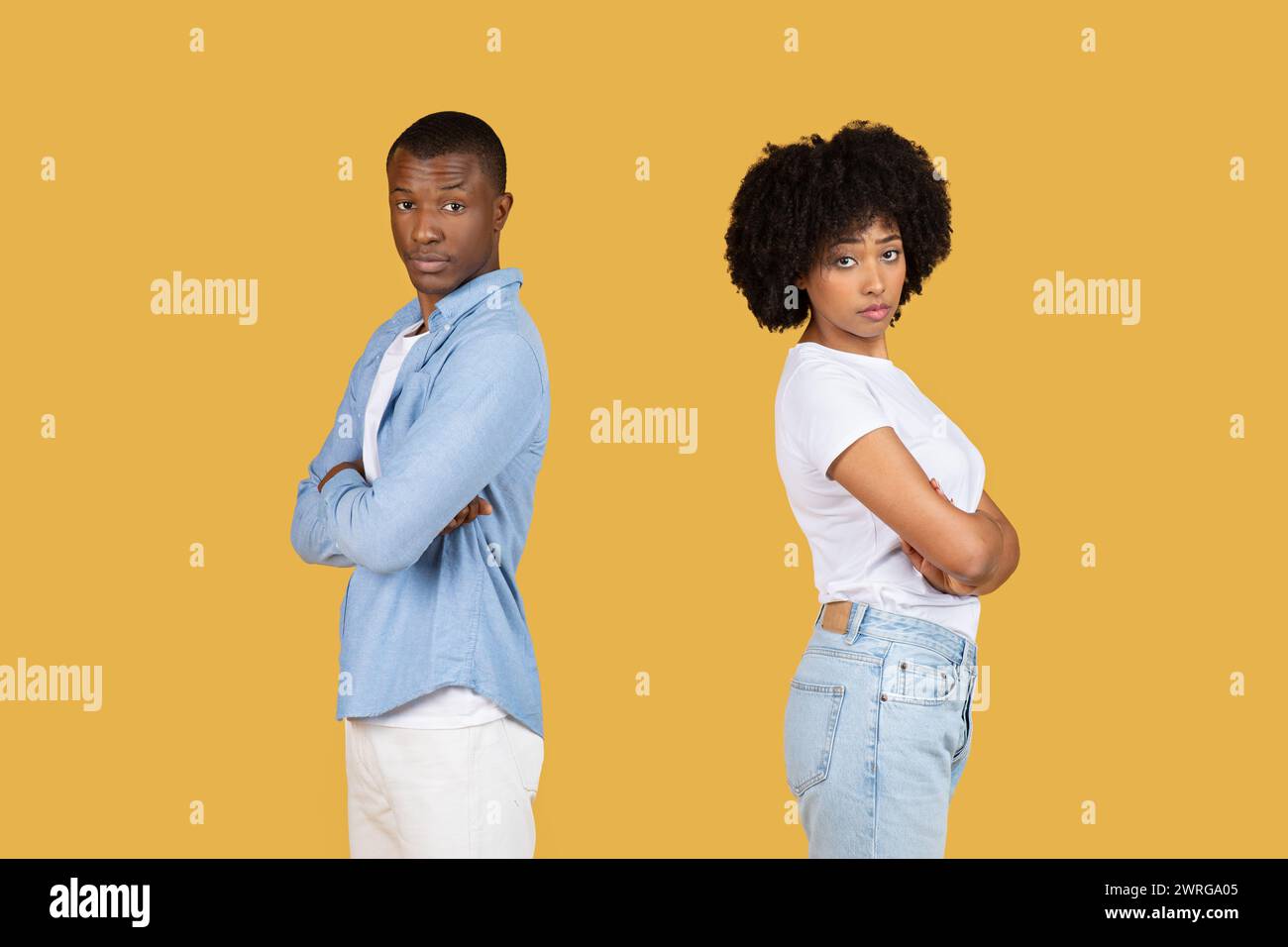 A young man and woman in casual clothing stand back to back with arms ...