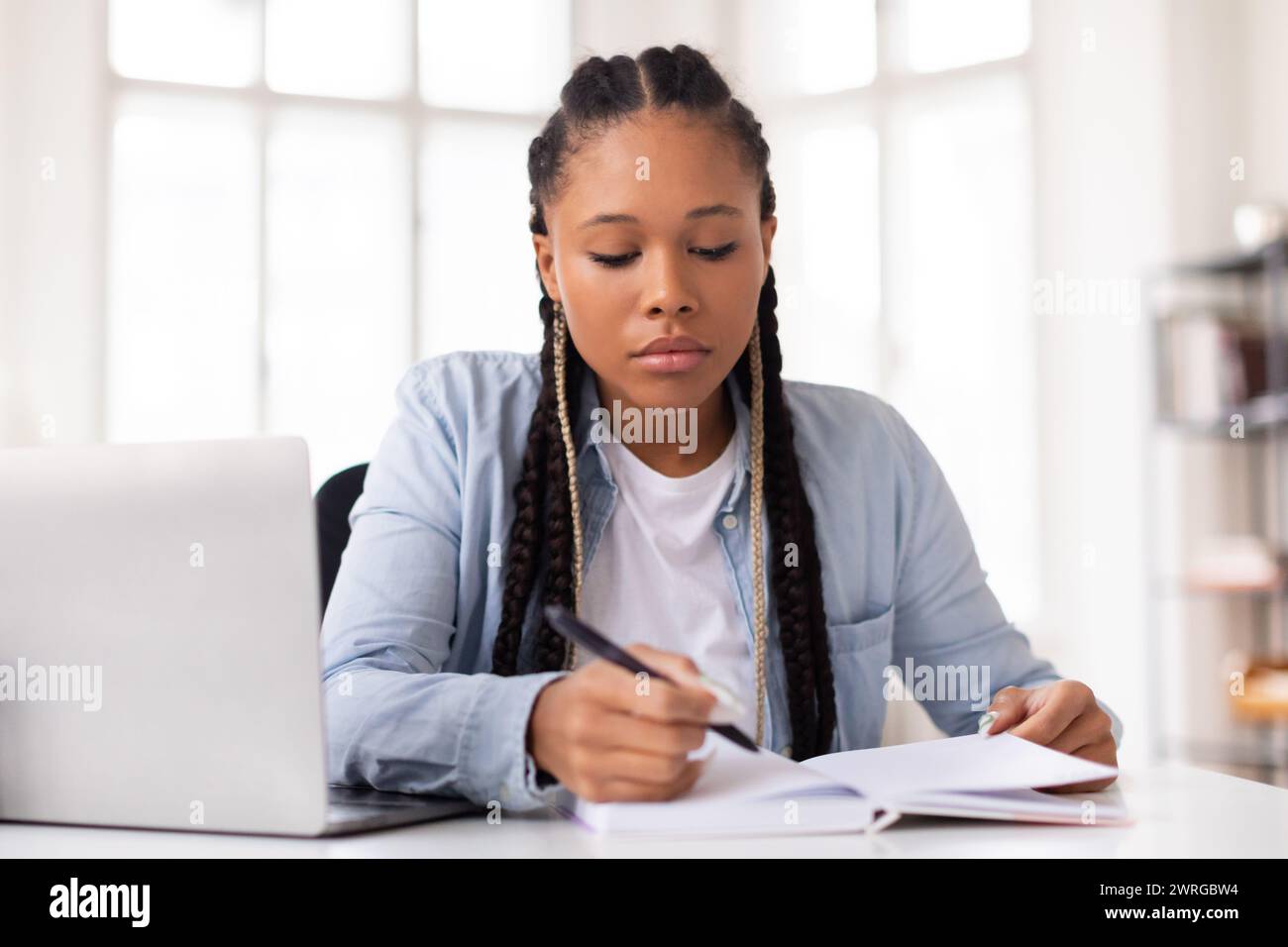 Concentrated black female student studying with laptop and notebook ...