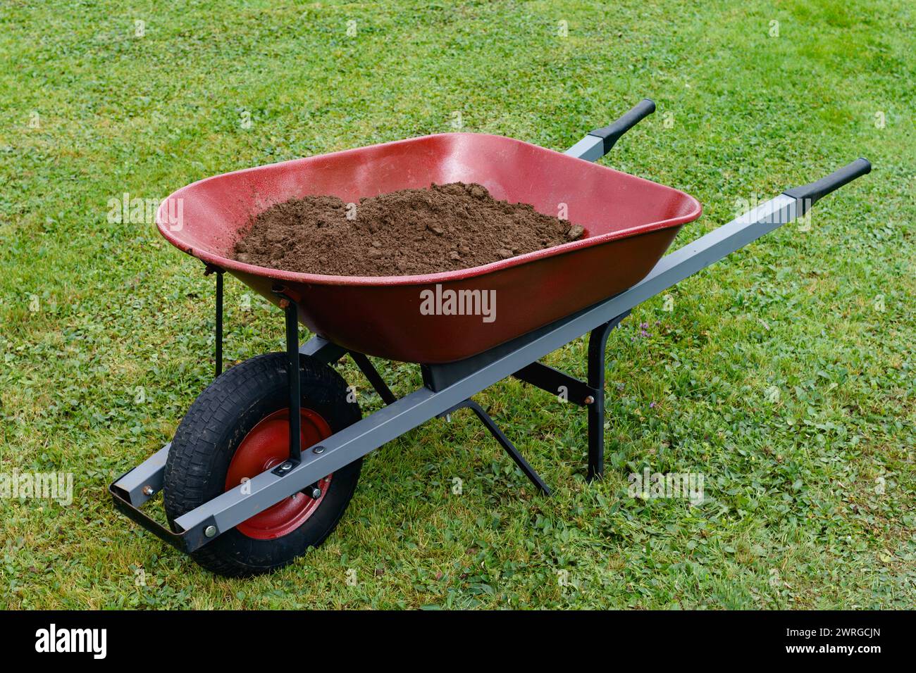 Red wheelbarrow and soil on yard lawn Stock Photo - Alamy
