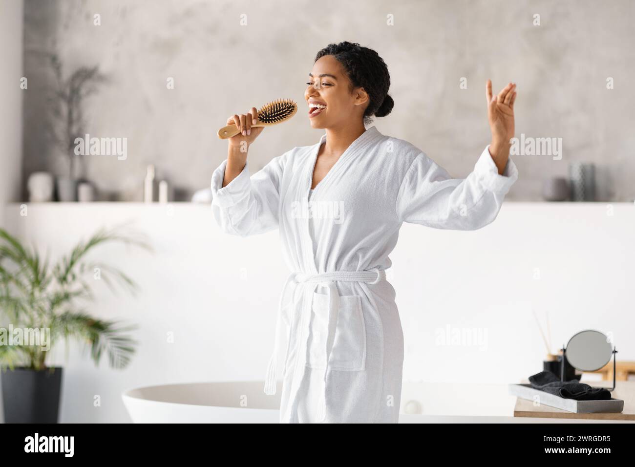 Happy young black woman holding hairbrush like microphone while singing ...